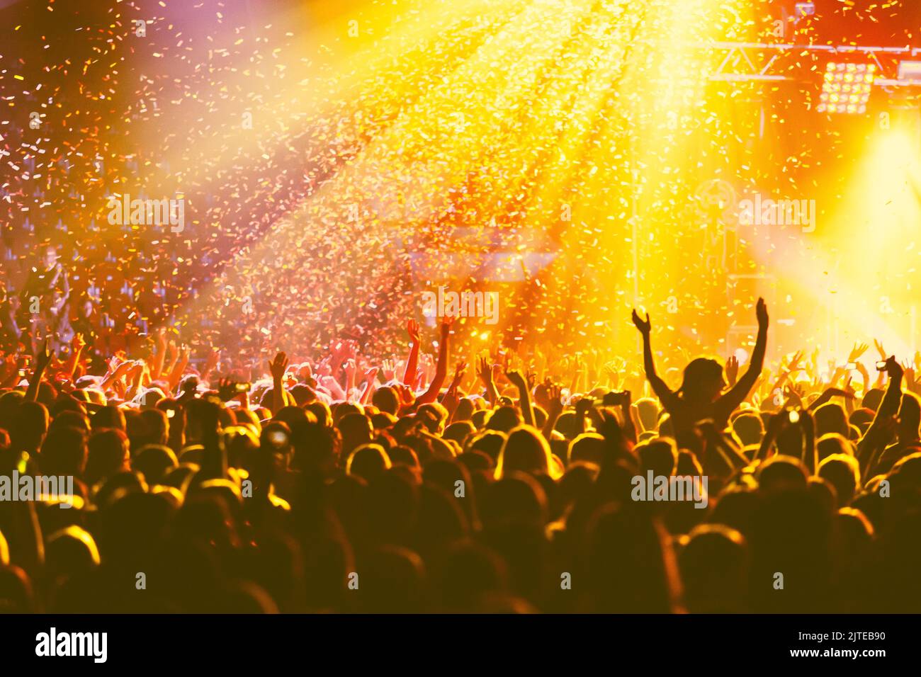 A crowded concert hall with scene stage orange and yellow lights, rock ...