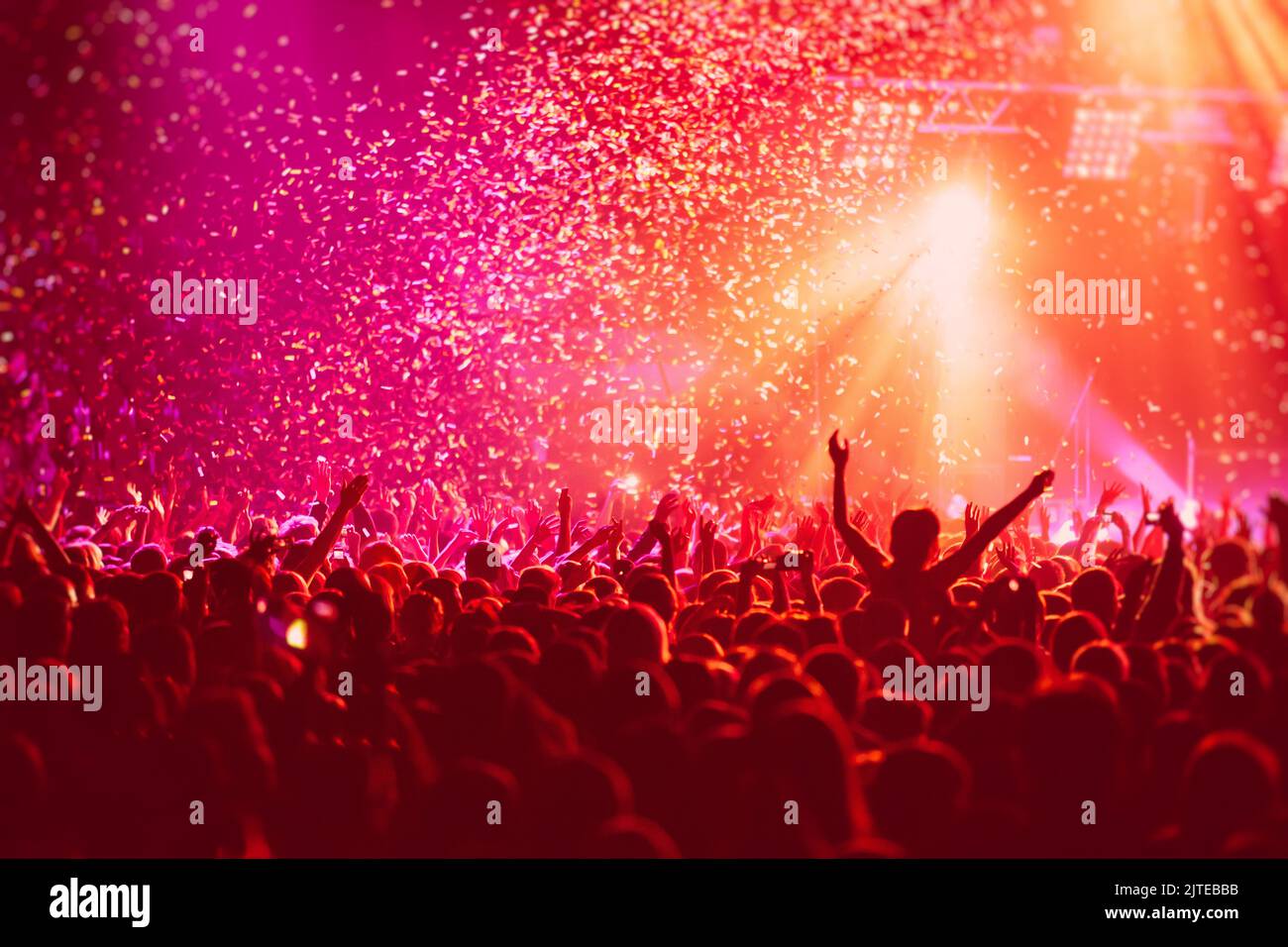 A crowded concert hall with scene stage in red lights, rock show ...
