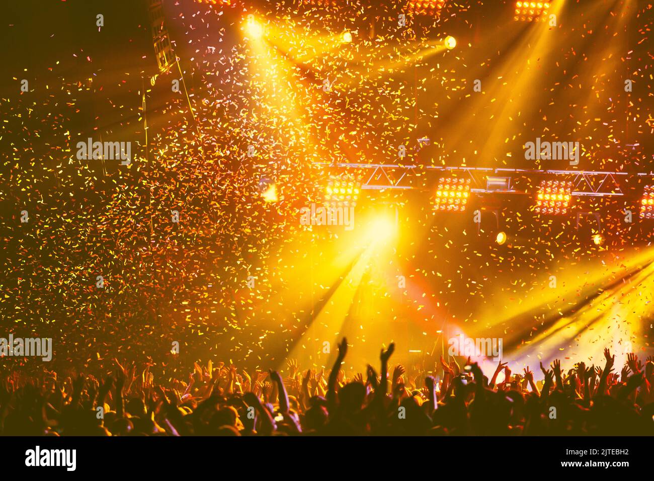 A crowded concert hall with scene stage orange and yellow lights, rock ...