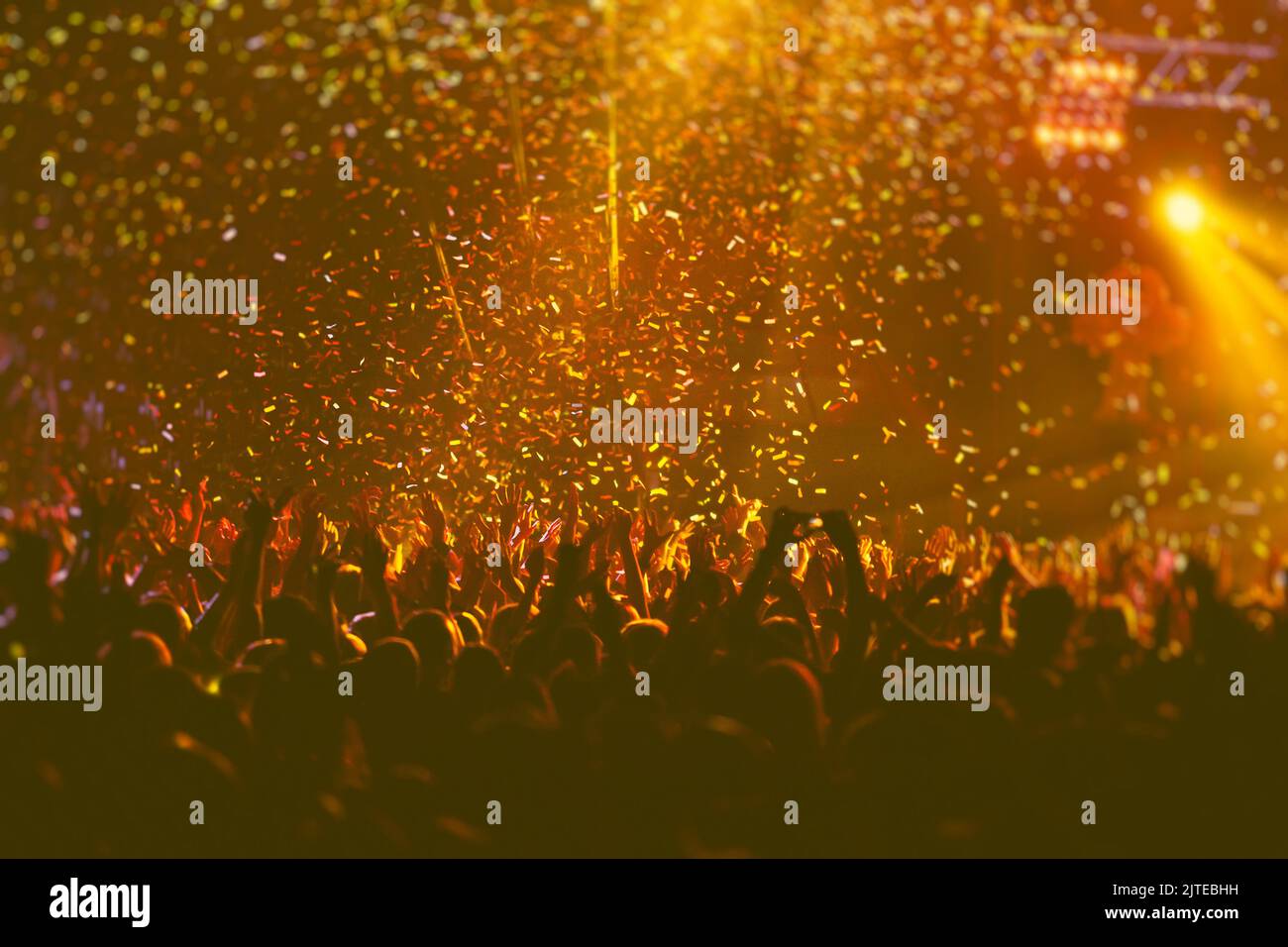 A crowded concert hall with scene stage orange and yellow lights, rock ...