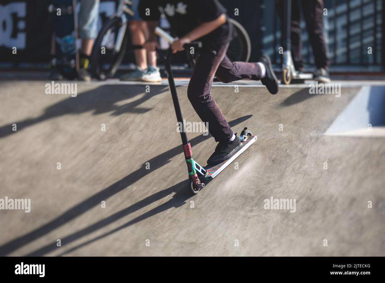 Skate park view with kids on a kick scooter doing tricks and stunts ...