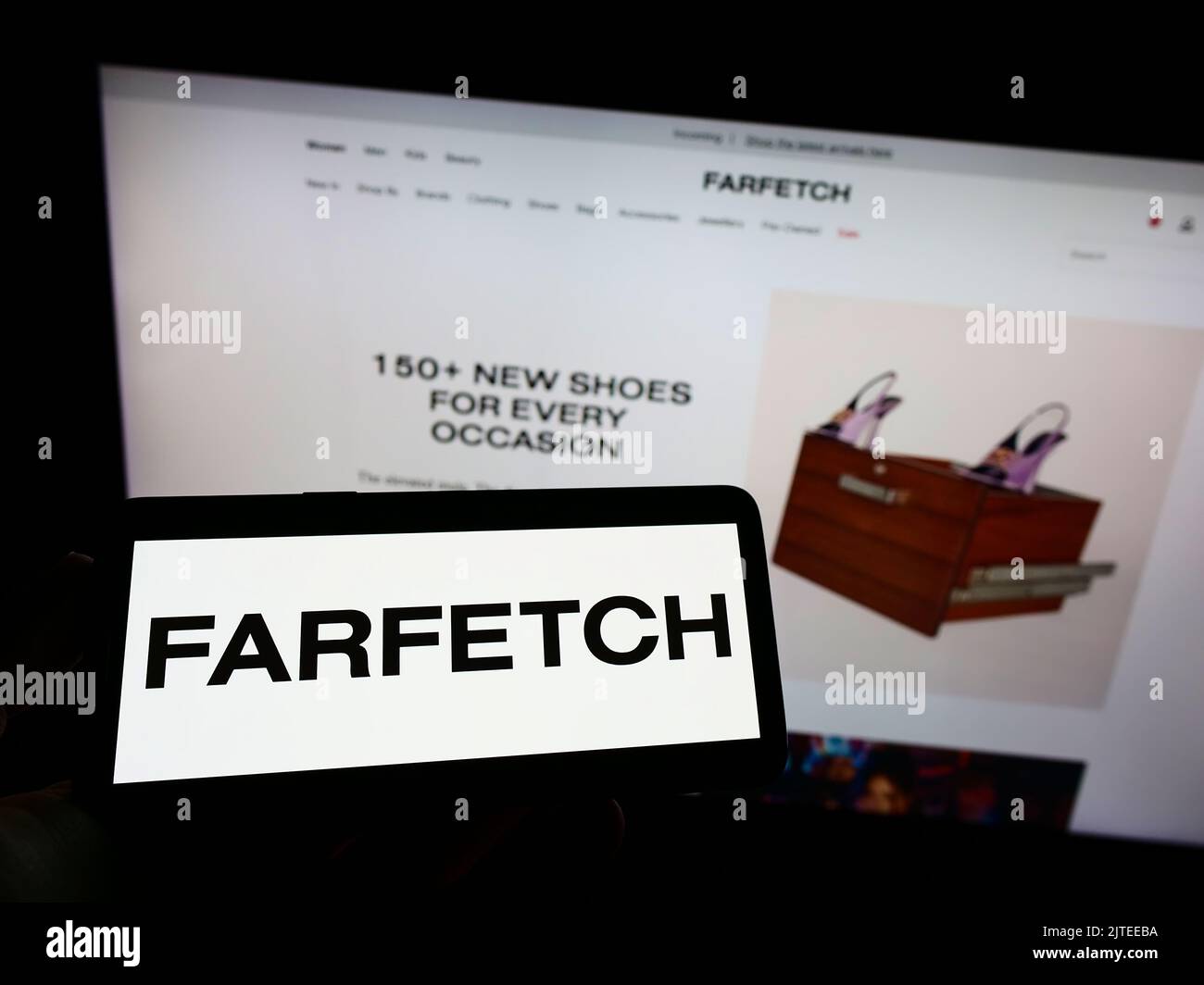 Person holding mobile phone with logo of British e-commerce company Farfetch Limited on screen ...