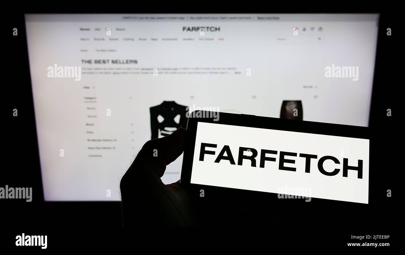 Person holding cellphone with logo of British e-commerce company Farfetch Limited on screen in ...