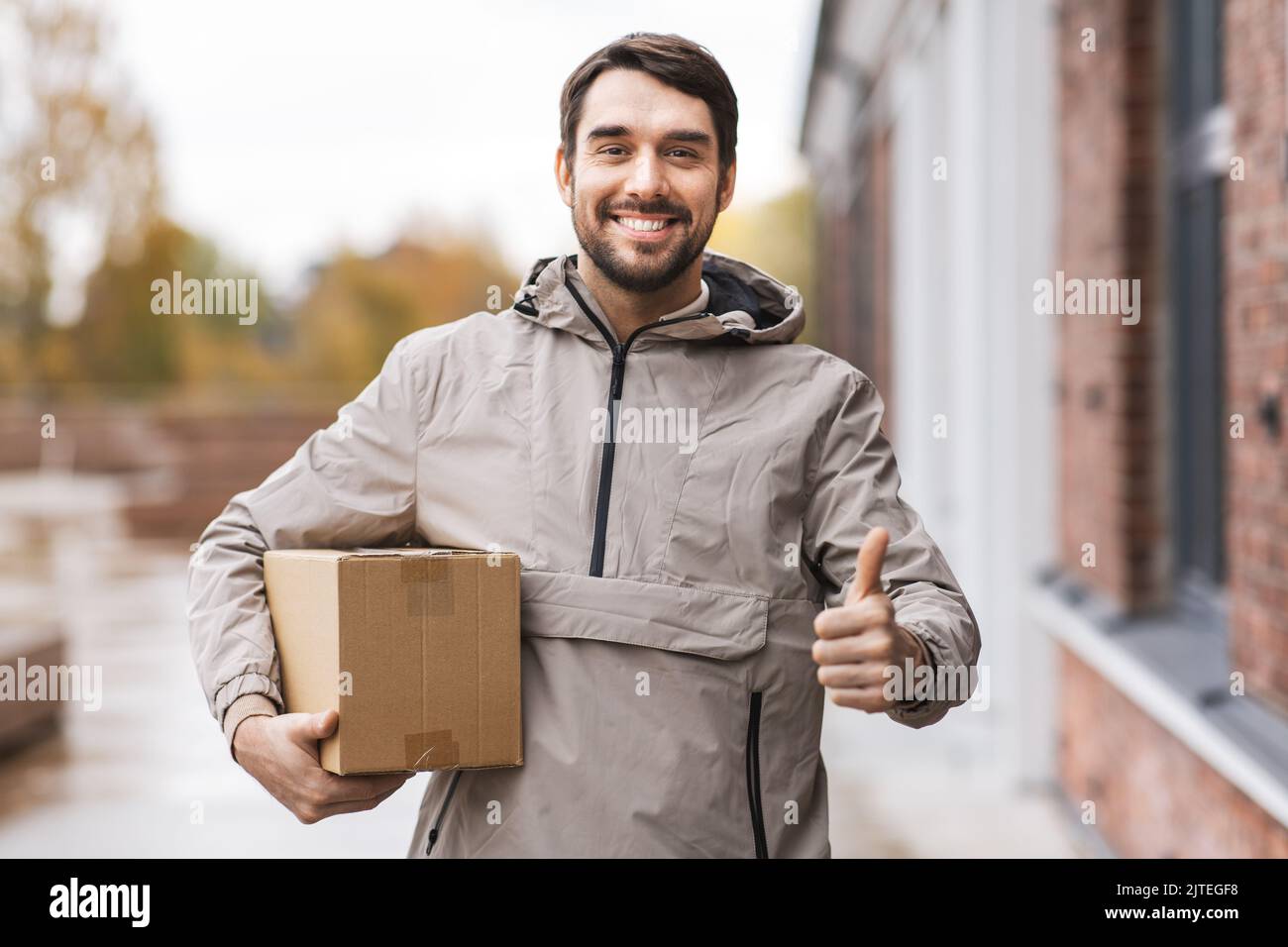 delivery man with parcel box showing thumbs up Stock Photo - Alamy