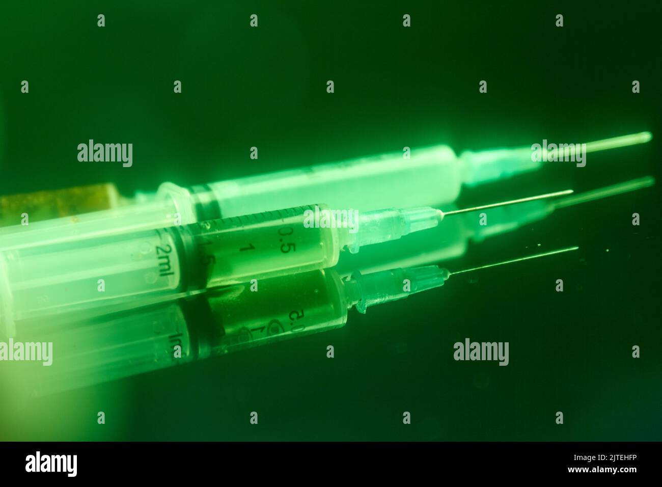 Close-up two syringes with green neon lighting. Reflective mirror ...