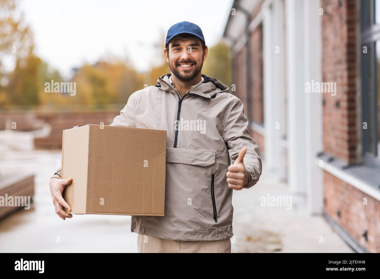 delivery man with parcel box showing thumbs up Stock Photo - Alamy