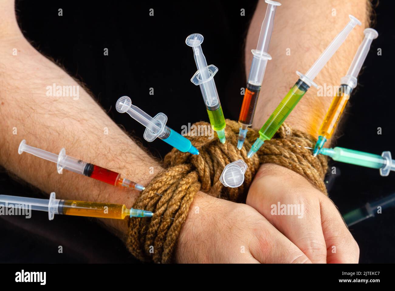 Close-up bound hands and colorful syringes stucked from it. Drug ...