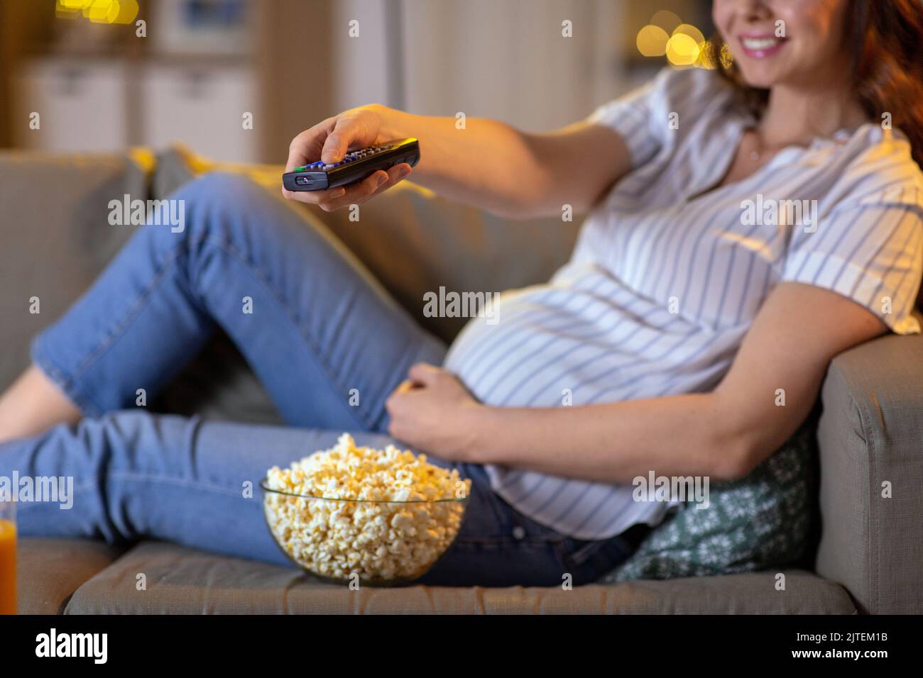 pregnant woman with remote control watching tv Stock Photo - Alamy