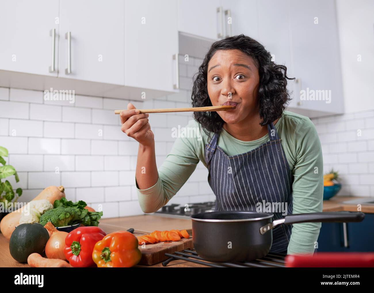 A young multiracial woman tastes her vegan cooking and is pleasantly ...
