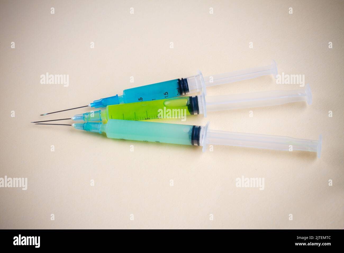 Close-up three colorful filled syringes on beige background. Drug use ...