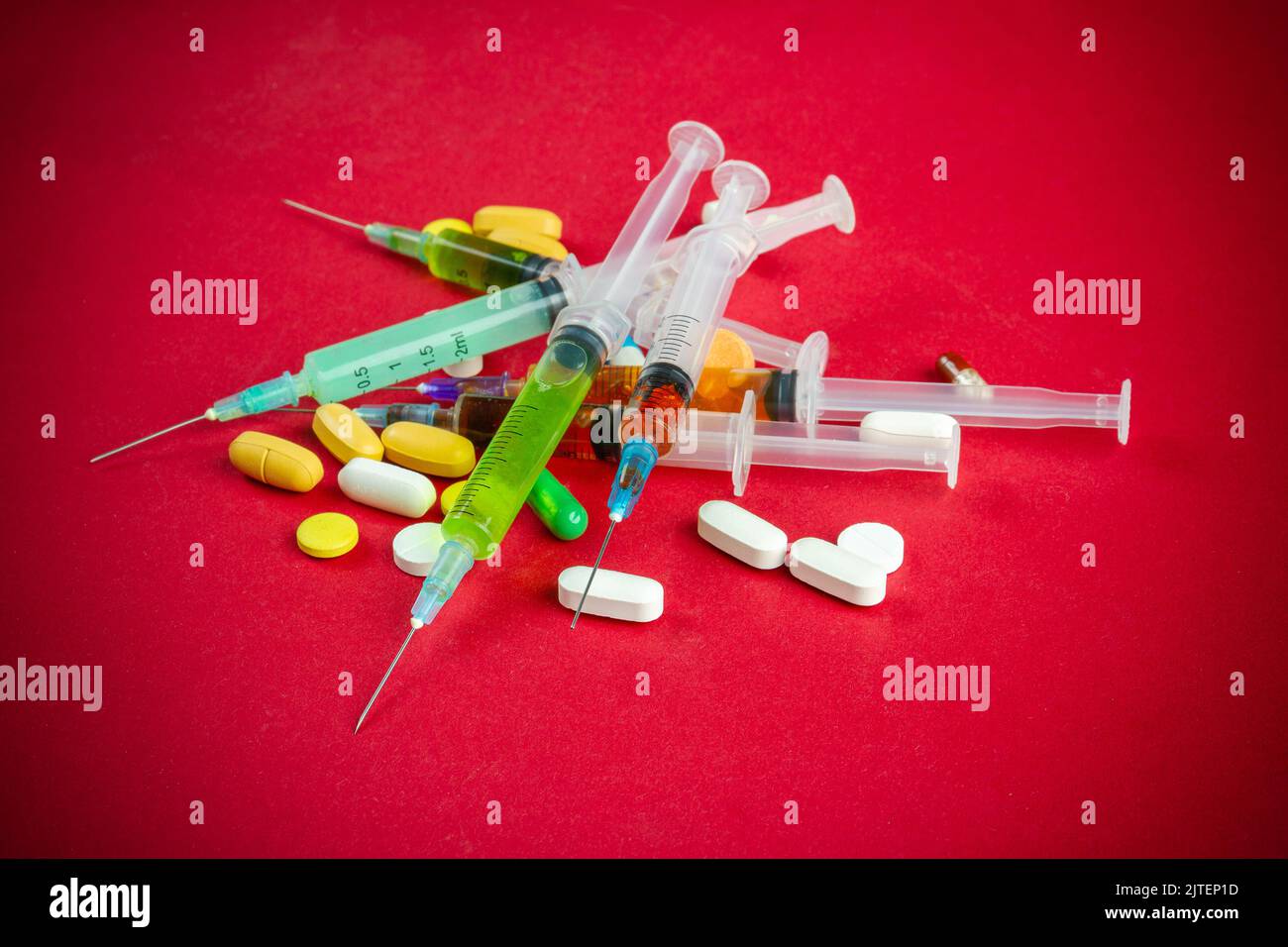 Pile of syringes and various colorful pills on red background. Drug ...