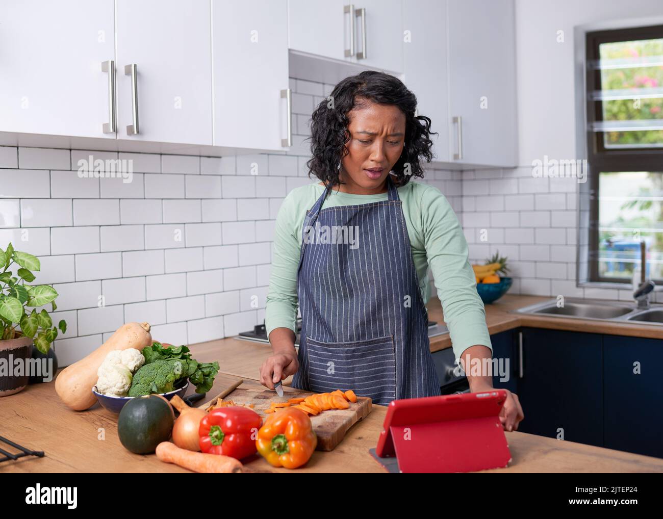 A young multiracial woman follows online recipe preparing dinner in the ...