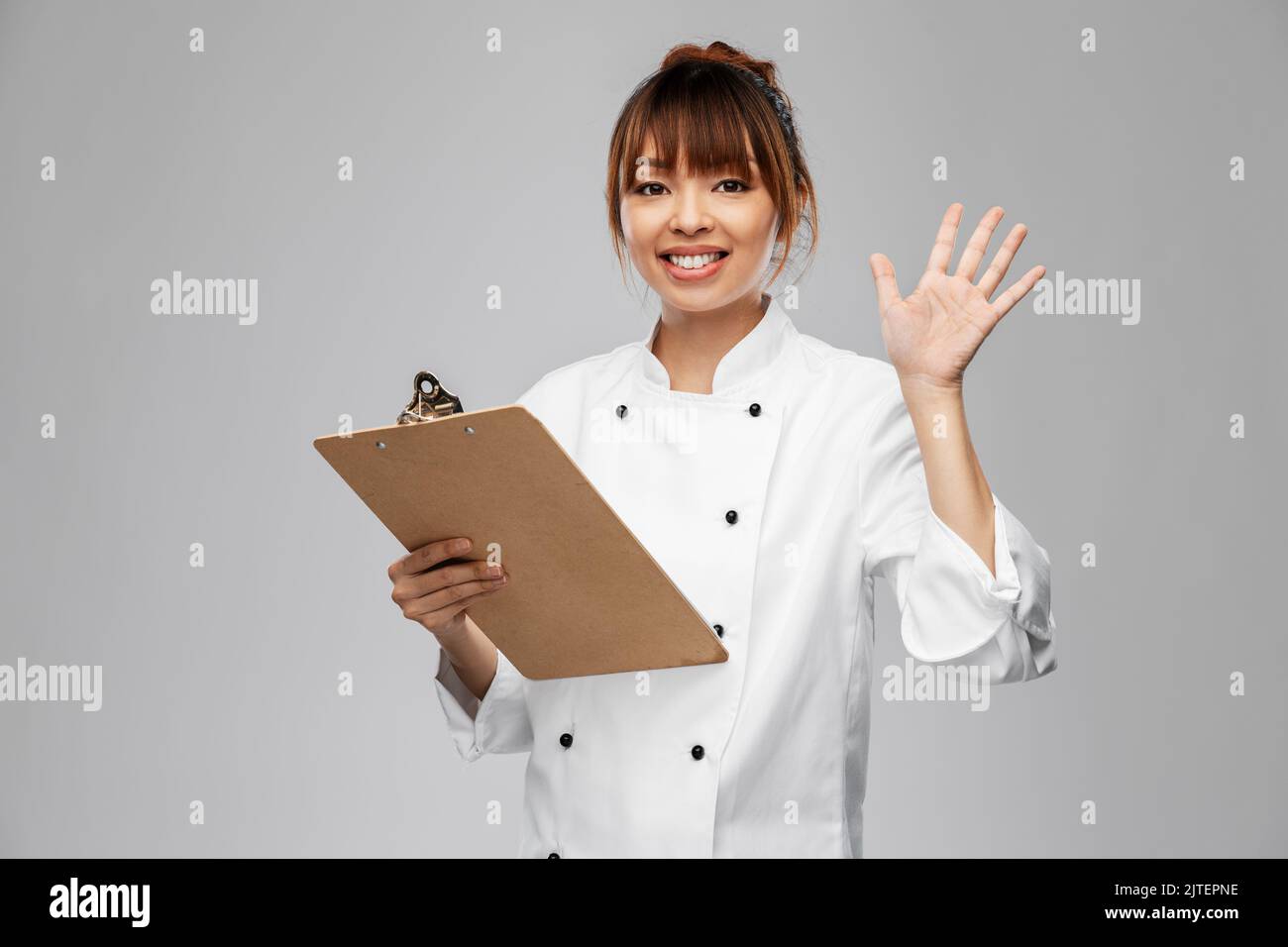 smiling female chef with clipboard waving hand Stock Photo - Alamy