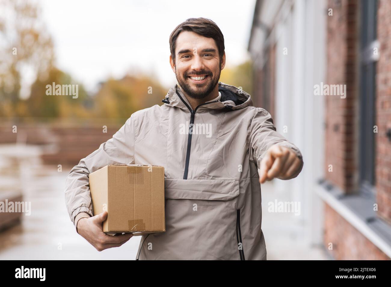 delivery man with parcel box pointing to camera Stock Photo - Alamy