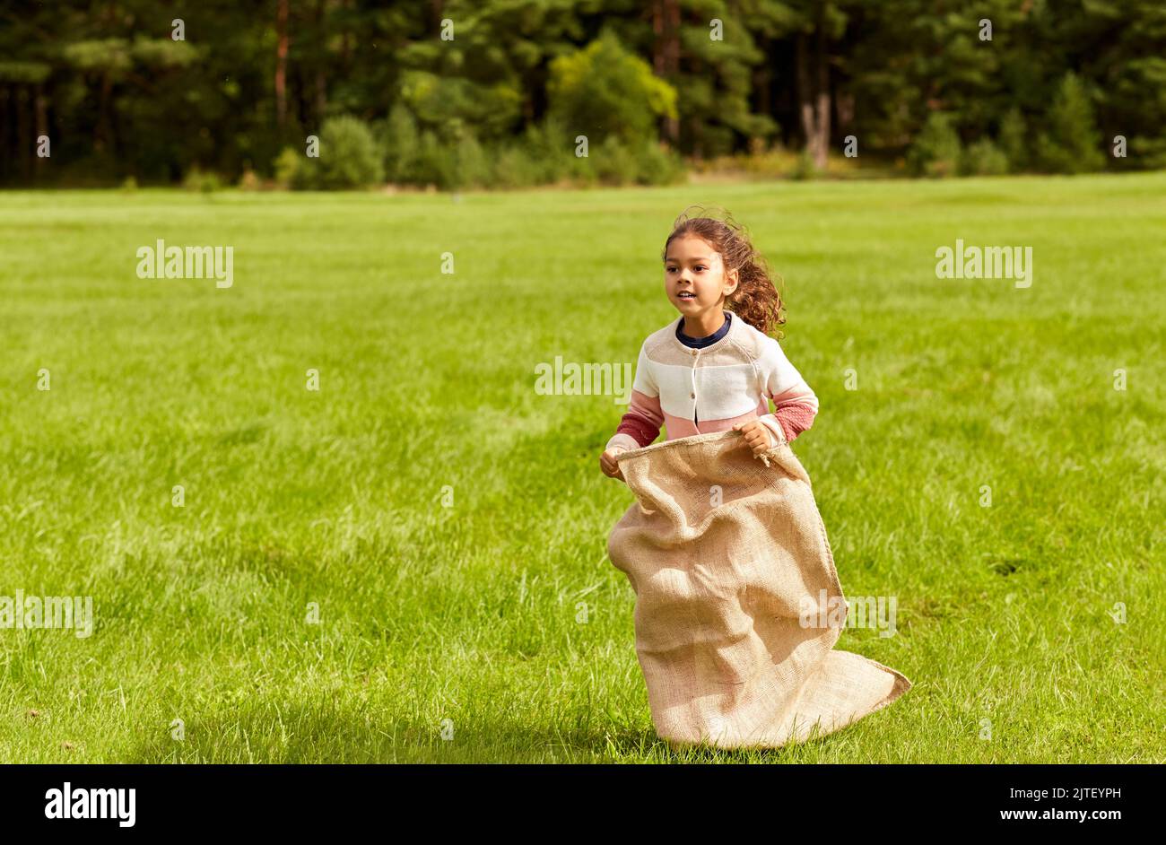 happy little girl playing bag jumping game at park Stock Photo - Alamy