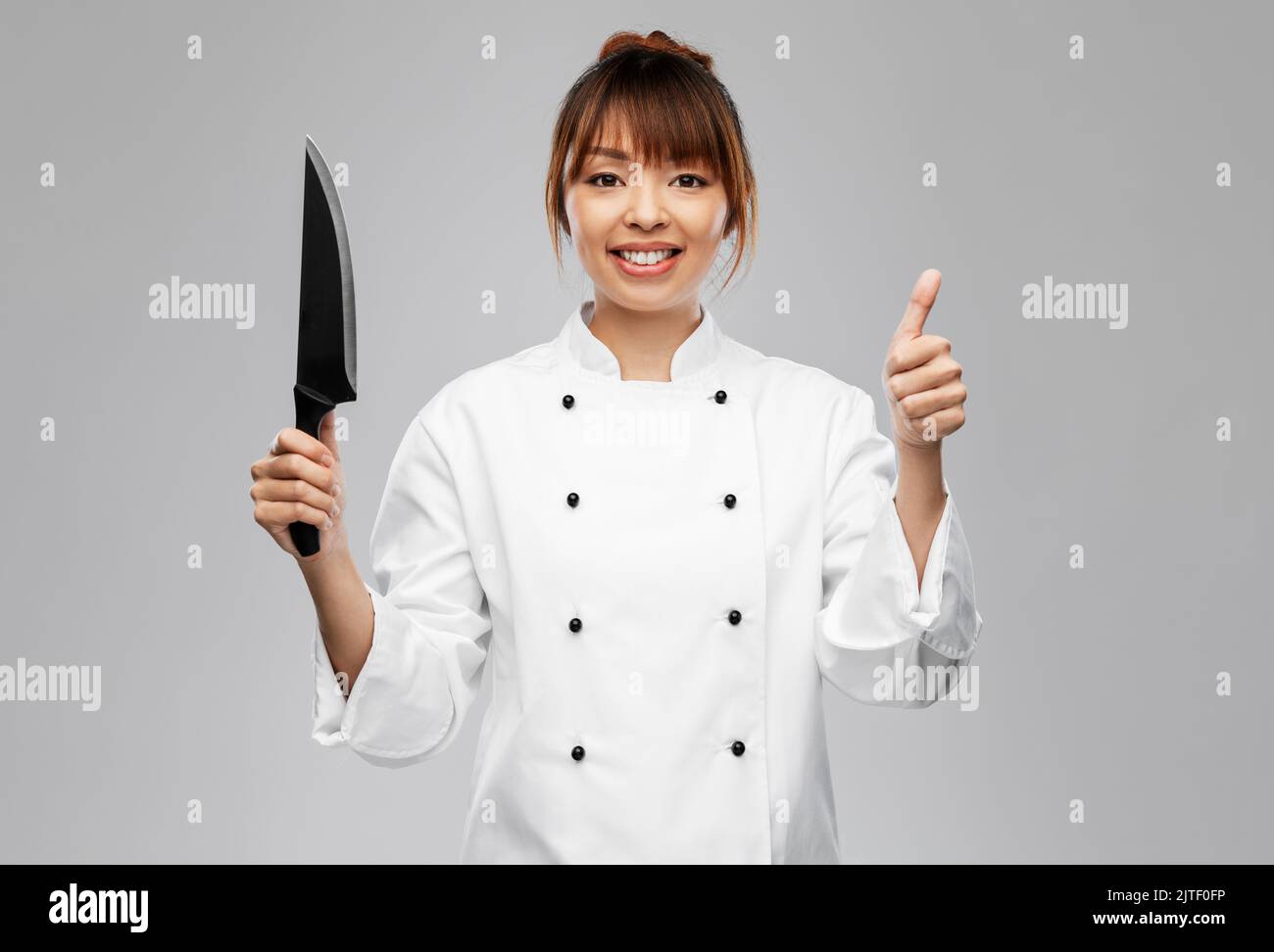 smiling female chef with knife showing thumbs up Stock Photo - Alamy
