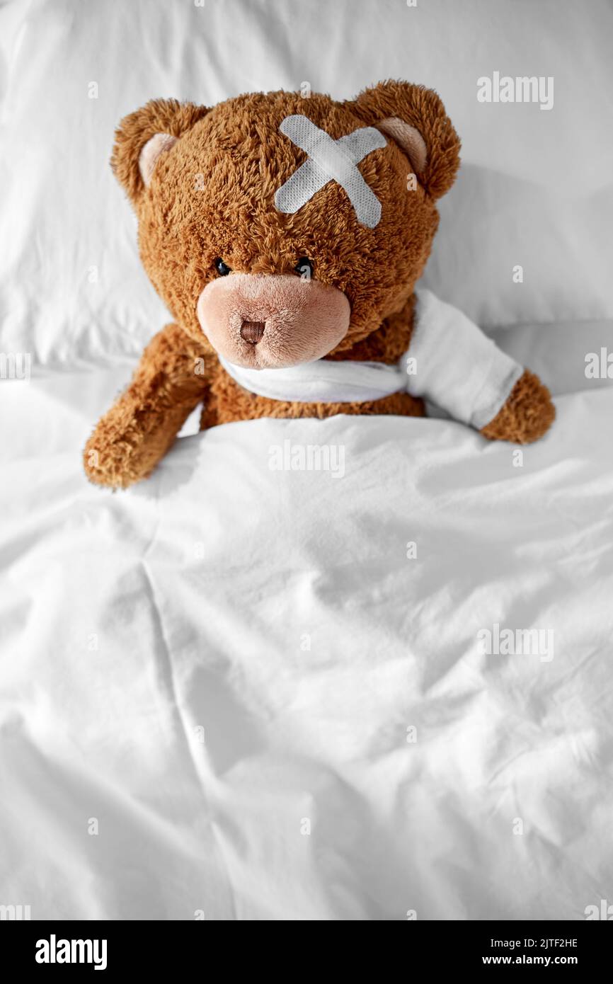 ill teddy bear with bandaged paw and head in bed Stock Photo - Alamy