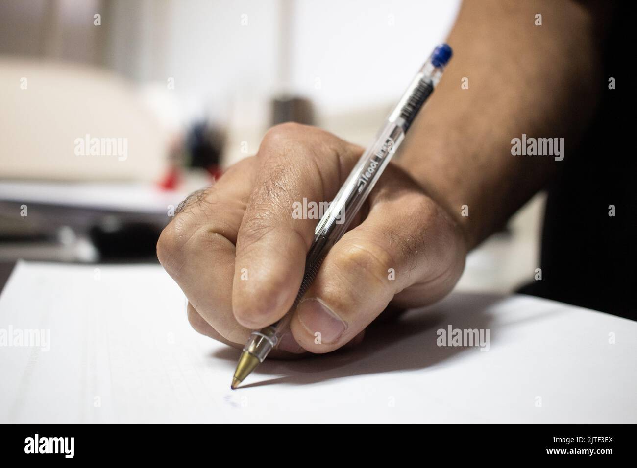 Hand with amputated index finger writing with a pen in a white paper ...