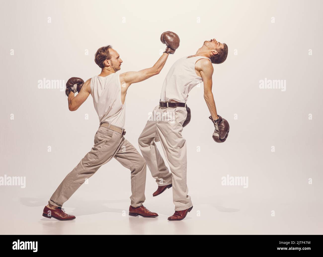 Portrait of two men playing, boxing in gloves isolated over grey studio ...