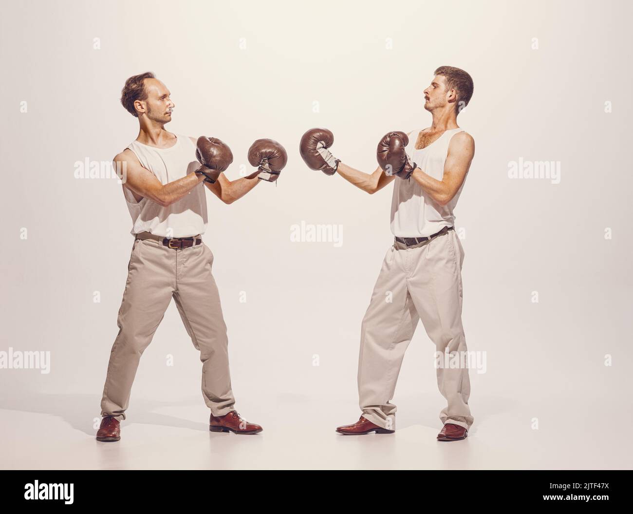 Portrait of two men playing, boxing in gloves isolated over grey studio ...