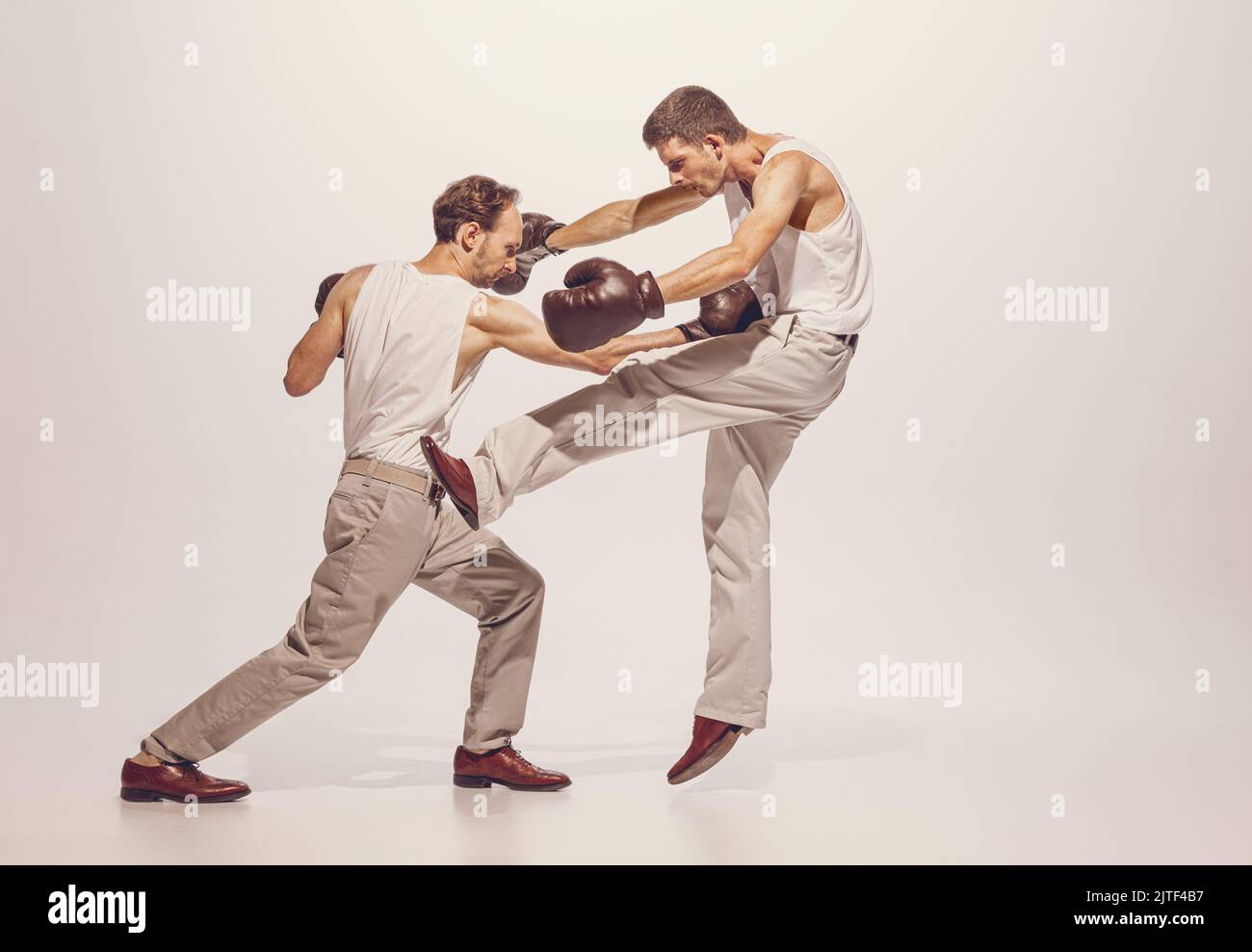 Portrait of two men playing, boxing in gloves isolated over grey studio ...