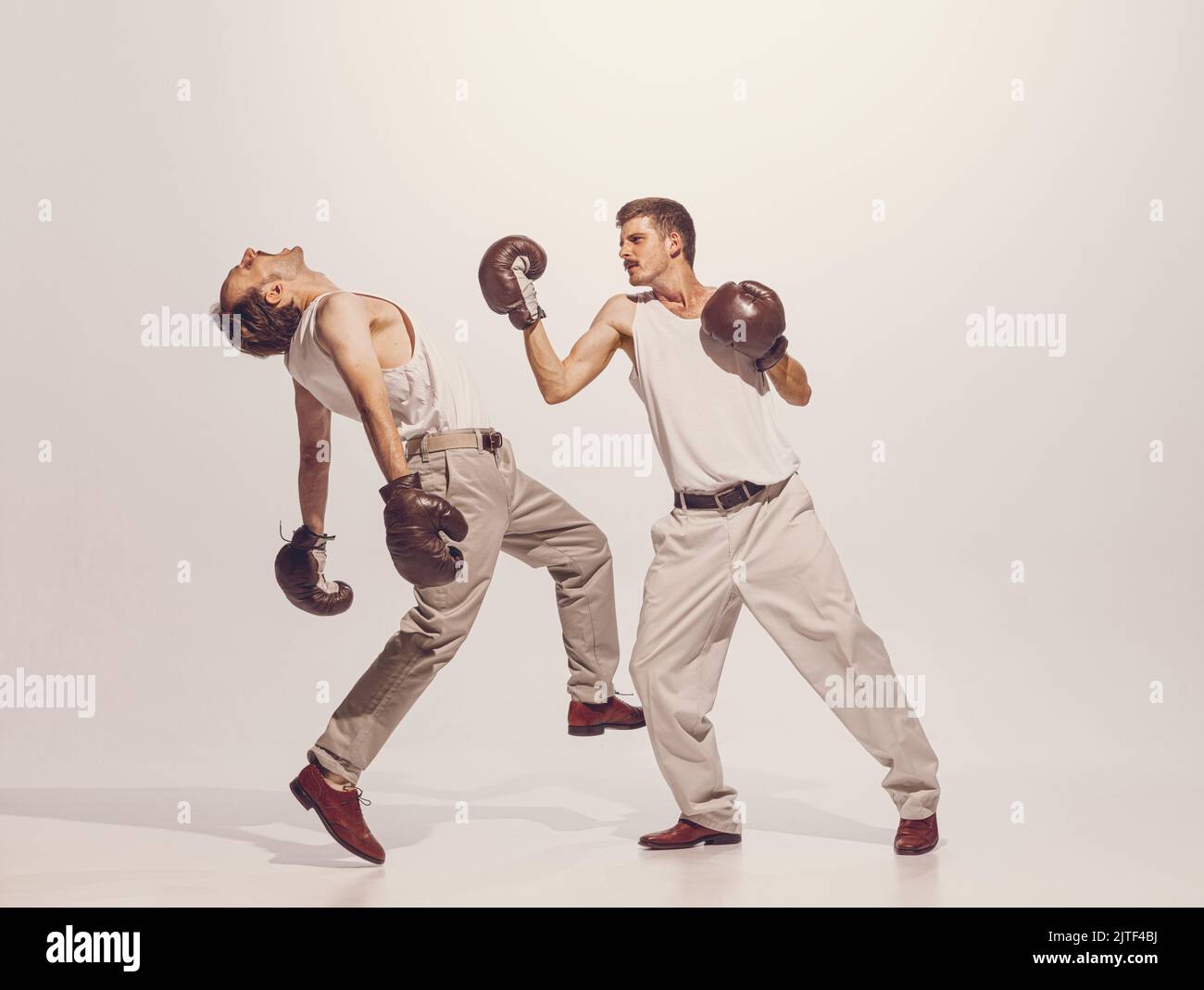 Portrait of two men playing, boxing in gloves isolated over grey studio ...