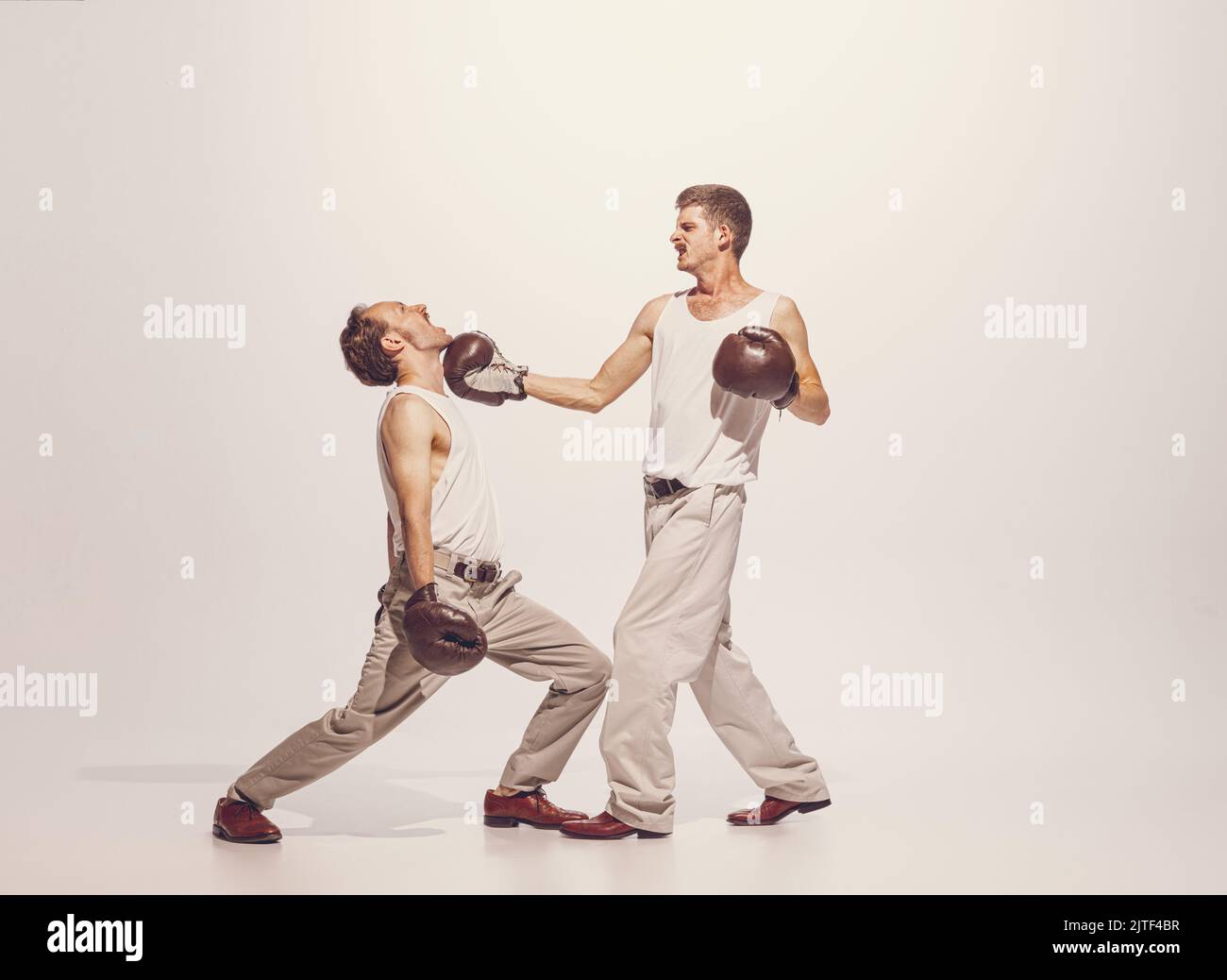 Portrait of two men playing, boxing in gloves isolated over grey studio ...
