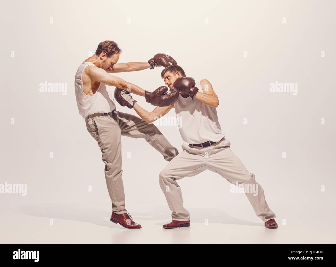Portrait of two men playing, boxing in gloves isolated over grey studio ...