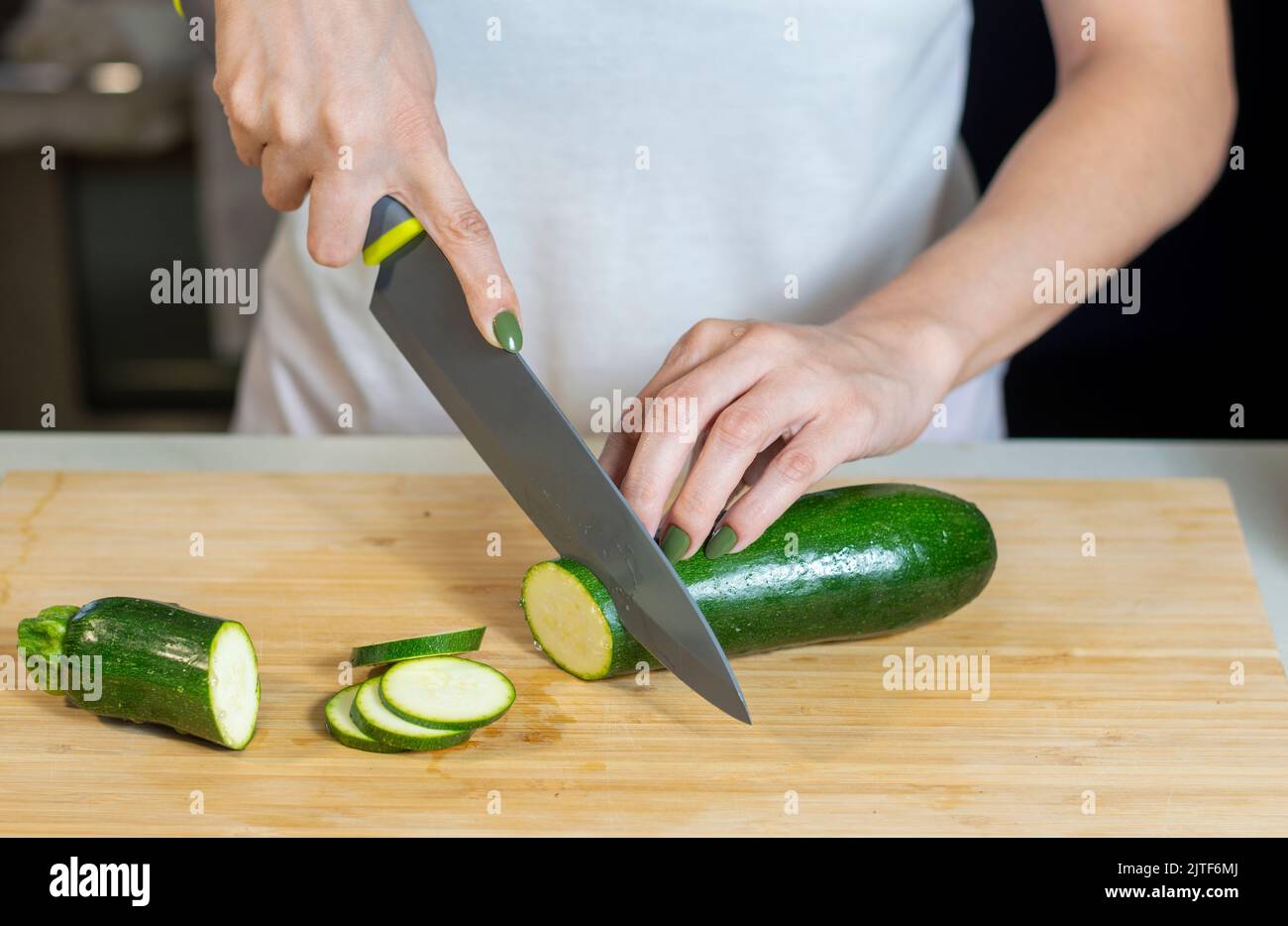 A close-up of young female hands cutting zucchini on a wooden cutting ...