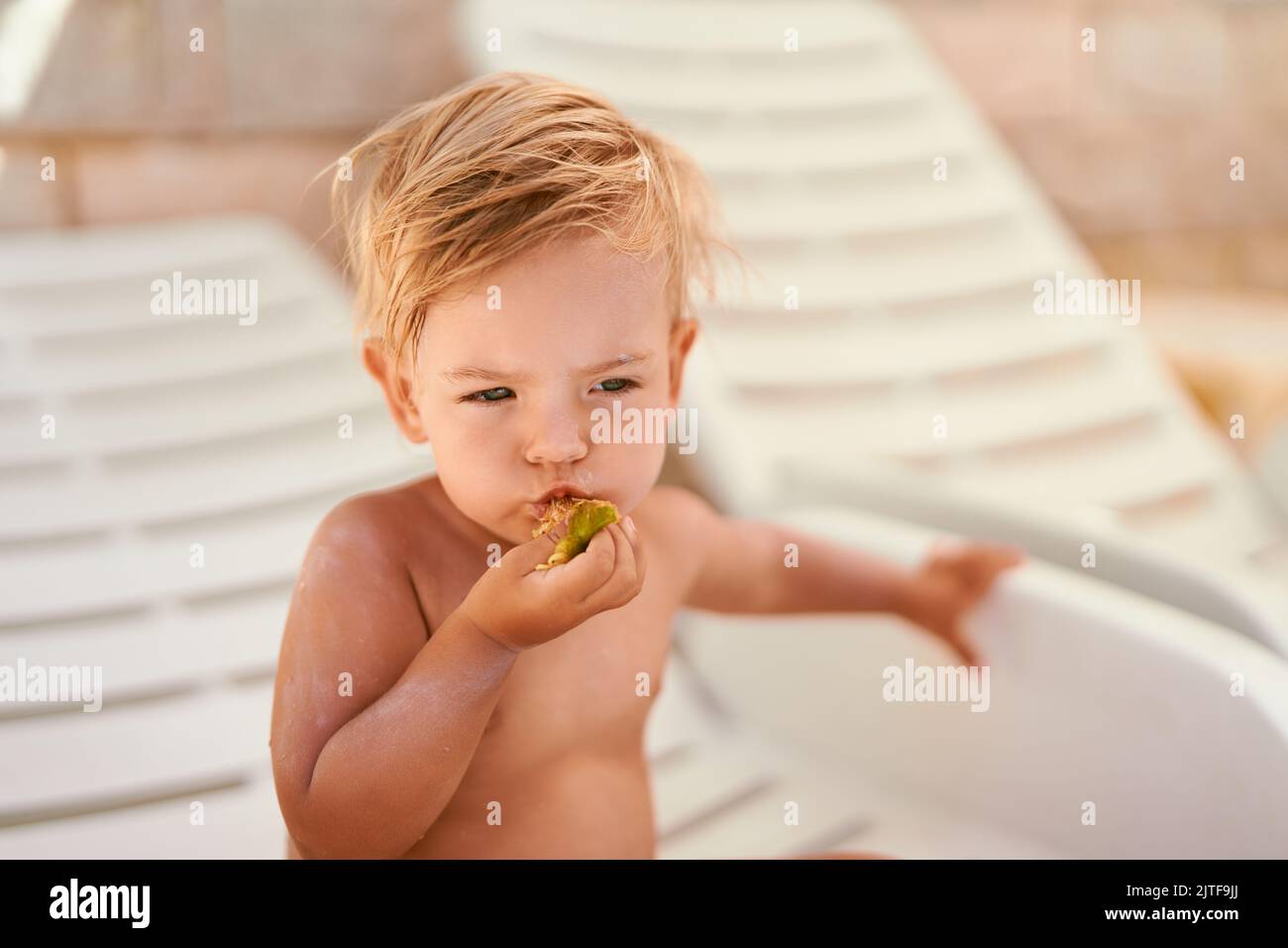 Little girl eating fruit while sitting on a sun lounger Stock Photo - Alamy