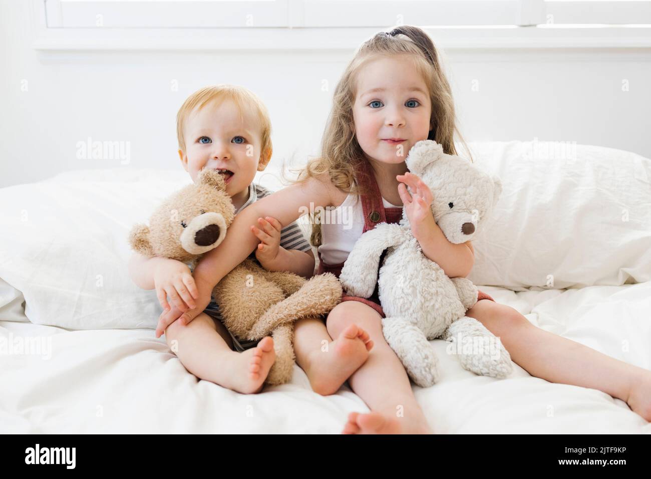 Portrait of brother (12-17 months) and sister (2-3) sitting on bed with ...