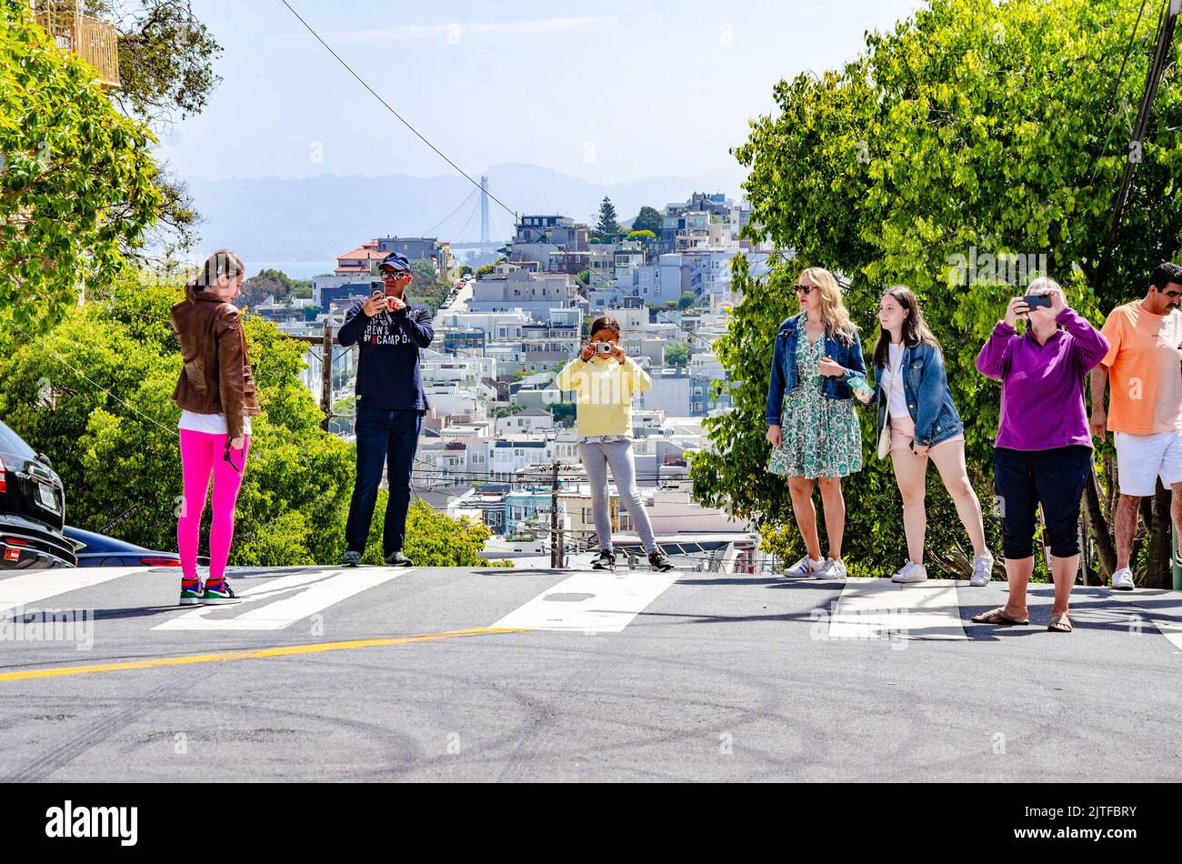 Tourists stand in the street watching and taking photographs of cars ...