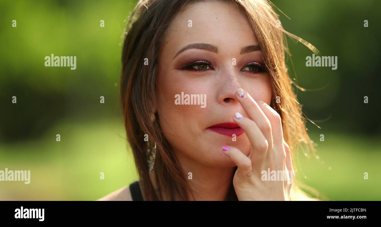 Pretty girl scratching face in outdoor park. Woman scratches lip ...