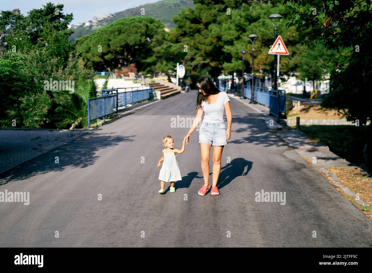 Budva, Montenegro - 12.07.22: Mom leads a little girl by the hand along ...