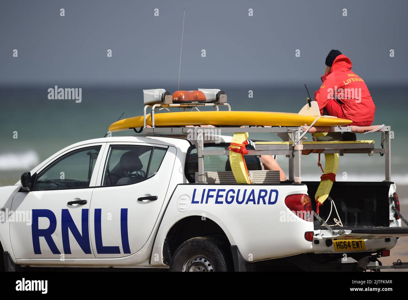 RNLI lifeguard sitting on vehicle on beach watching surfing competition ...