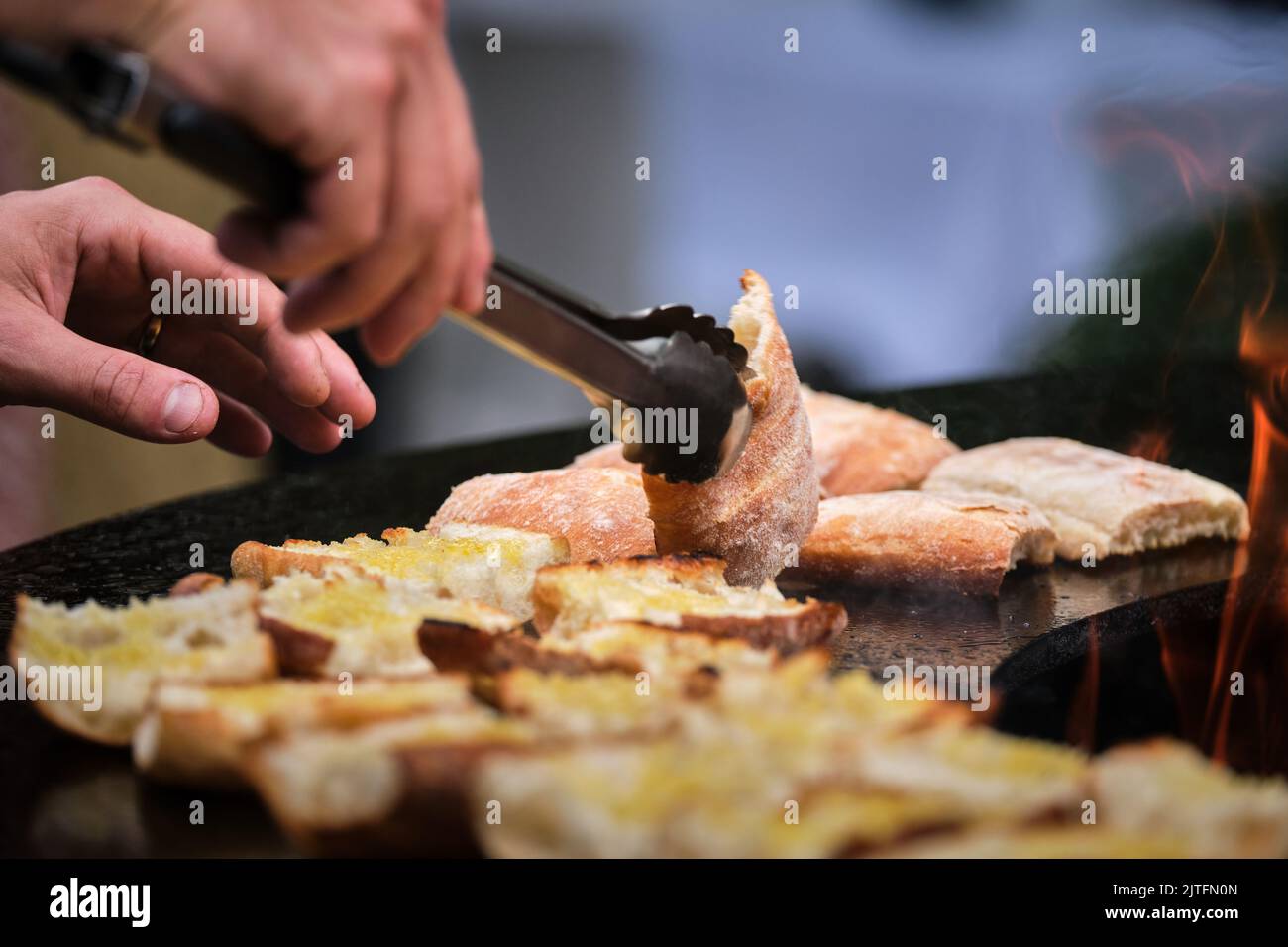 close-up detail view of chef flipping sandwiches grilled at round steel ...