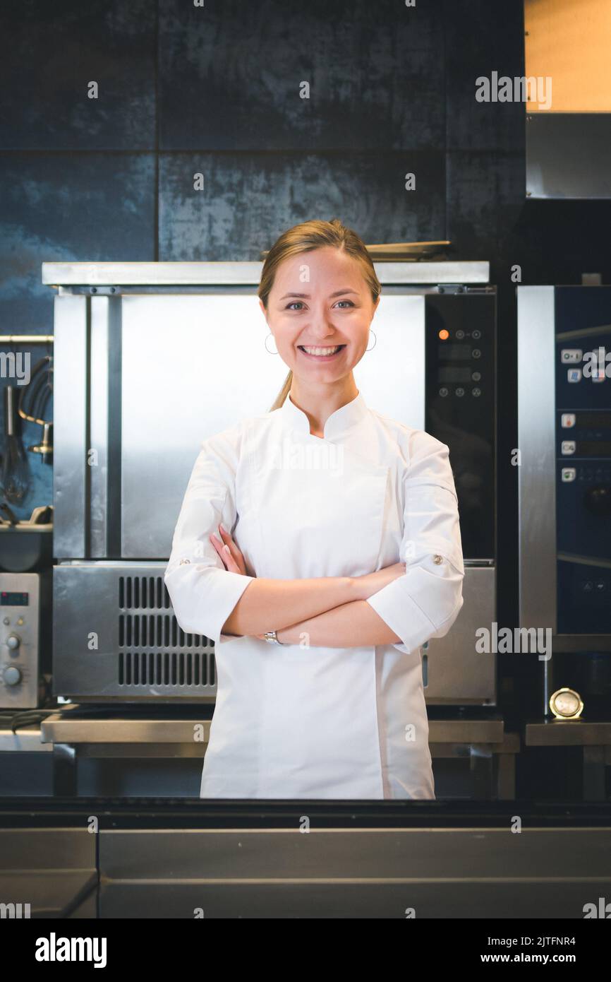 Portrait of confident and smiling young woman chef dressed in white ...