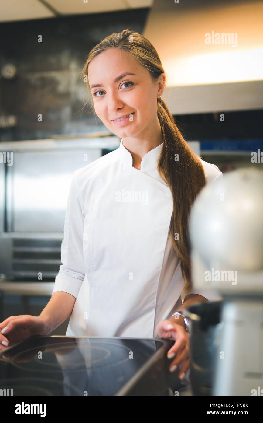 Portrait of confident and smiling young woman chef dressed in white ...