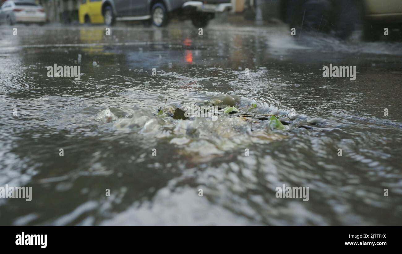 A stream of rainwater flows into the storm drain cars are driving in ...