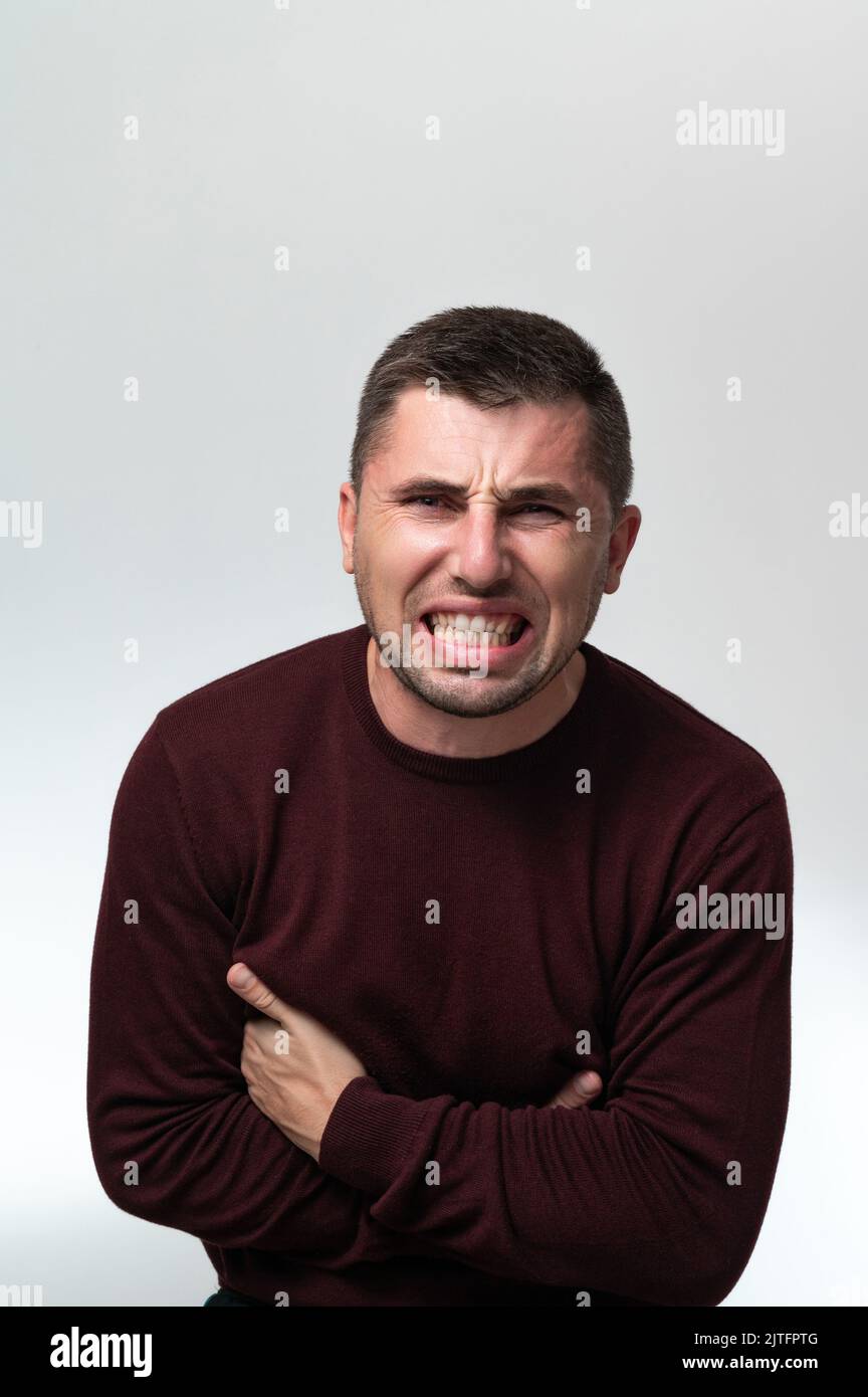 A man touches his stomach with two hands, on a white background with ...