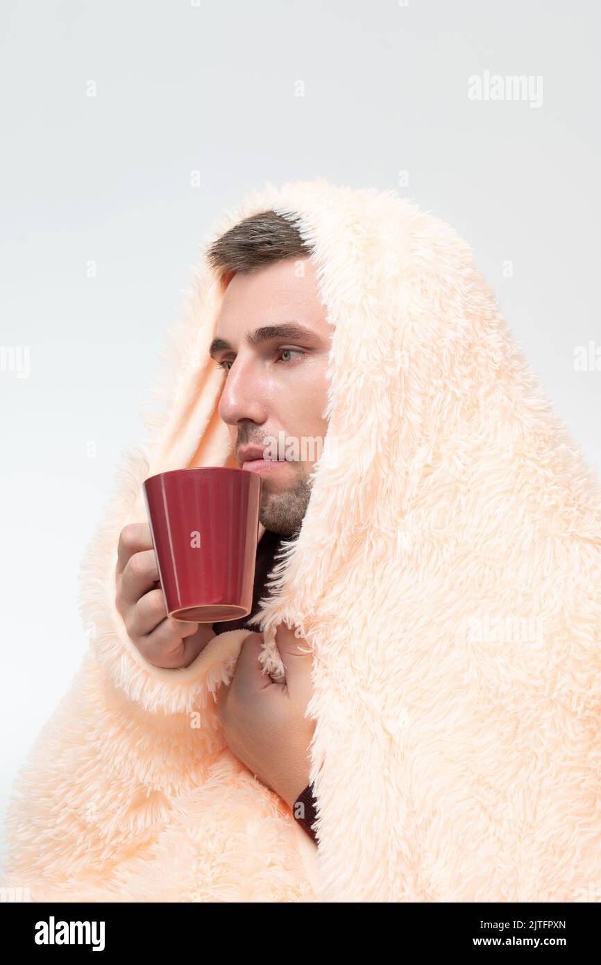 A man is wrapped in a blanket, holding a mug with a drink in his hands ...