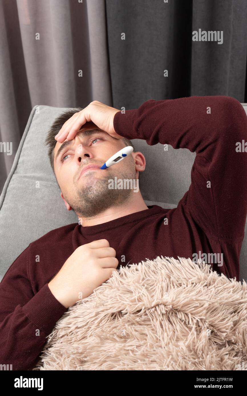 Man measures temperature and holds hand to head because of headache ...