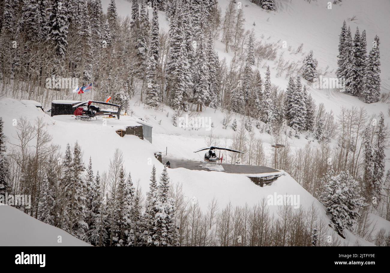 A helicopter sits on a landing pad surrounded by snow in the mountains ...