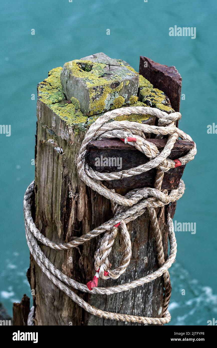 old discarded rope twisted around a weather beaten wooden pile or ...