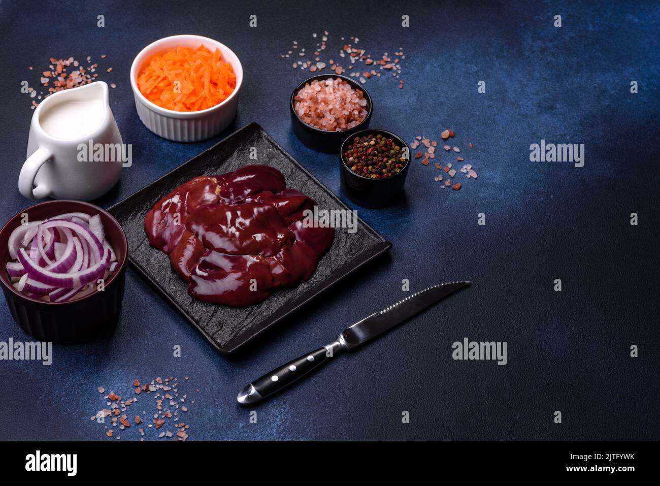 Pieces of raw liver on a wooden cutting board against a dark concrete ...