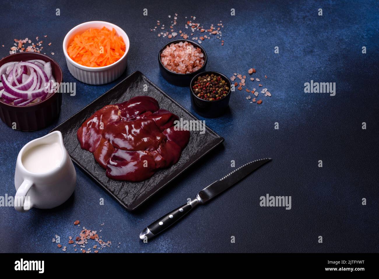 Pieces of raw liver on a wooden cutting board against a dark concrete ...
