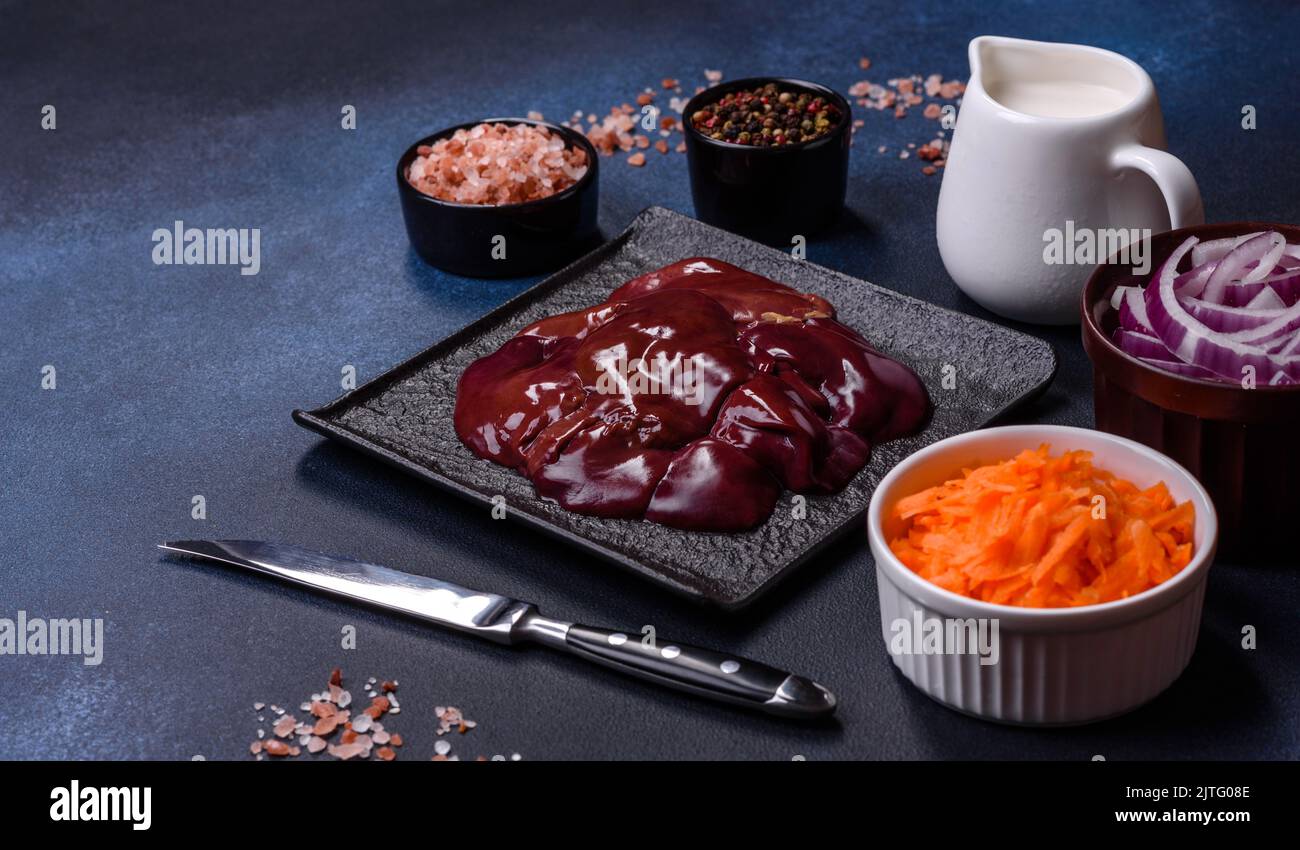 Pieces of raw liver on a wooden cutting board against a dark concrete ...