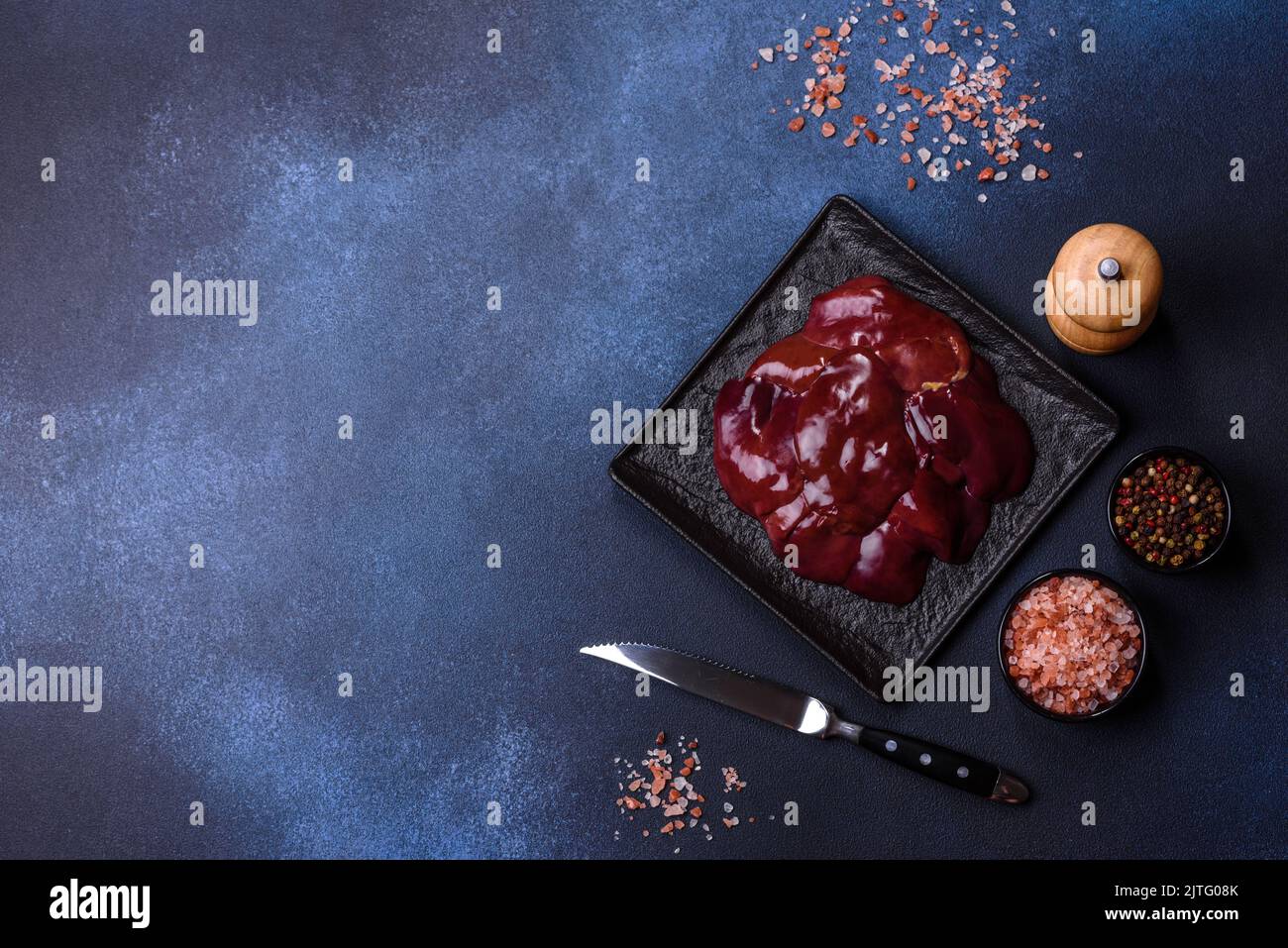 Pieces of raw liver on a wooden cutting board against a dark concrete ...