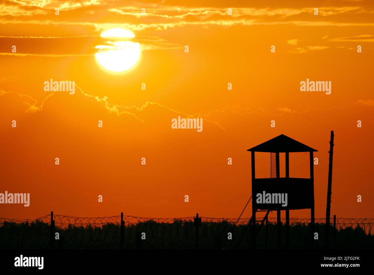 Fence with barbed wire and an old watchtower background bright sun and ...