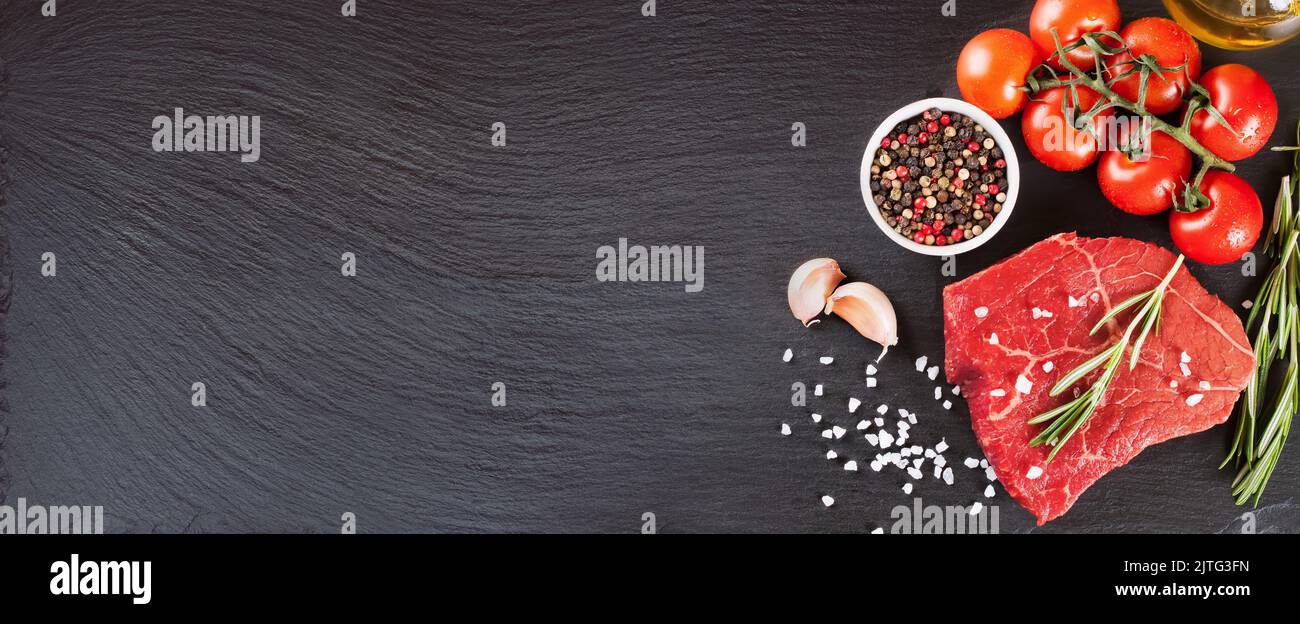 Raw beef steak with spices and ingredients for cooking on black slate ...